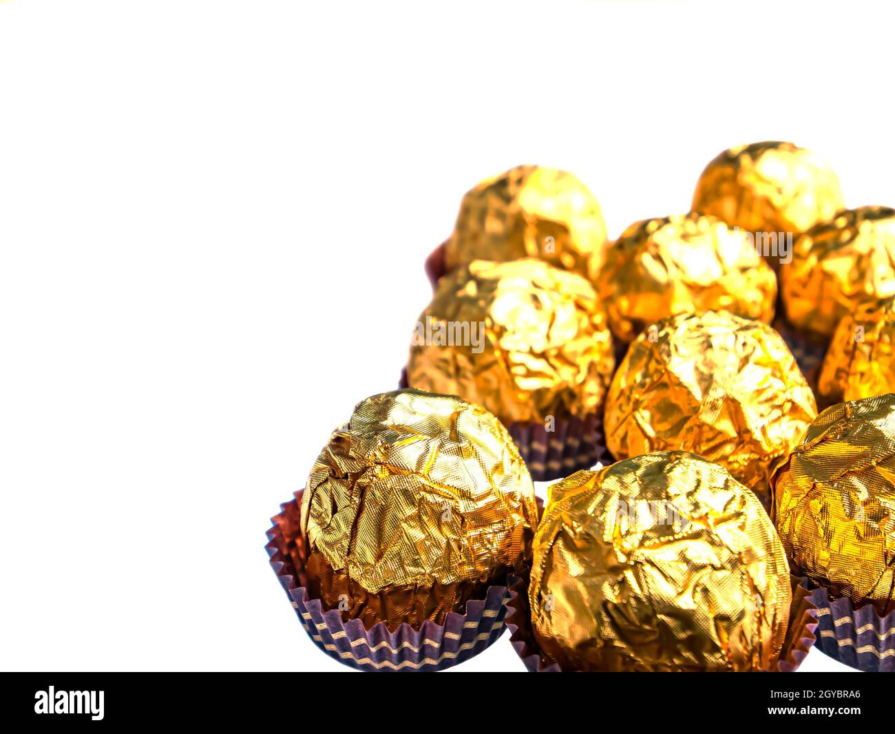 Round chocolate candies in a golden foil wrapper on a white background ...