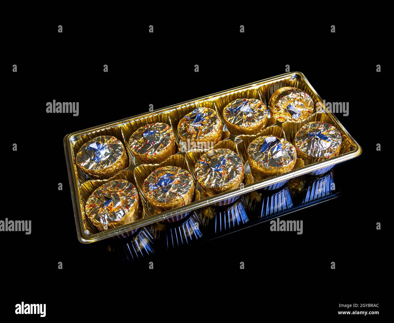 A box of round candies in golden foil on a black background. Wrapped ...