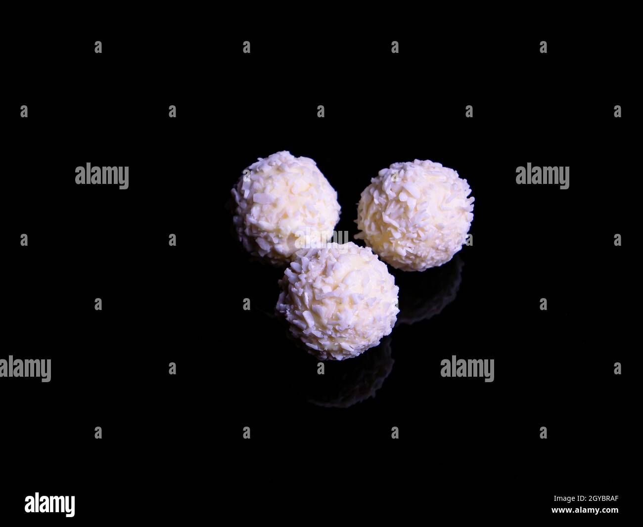 Round white candy with coconut flakes on a black background. Chocolate ...