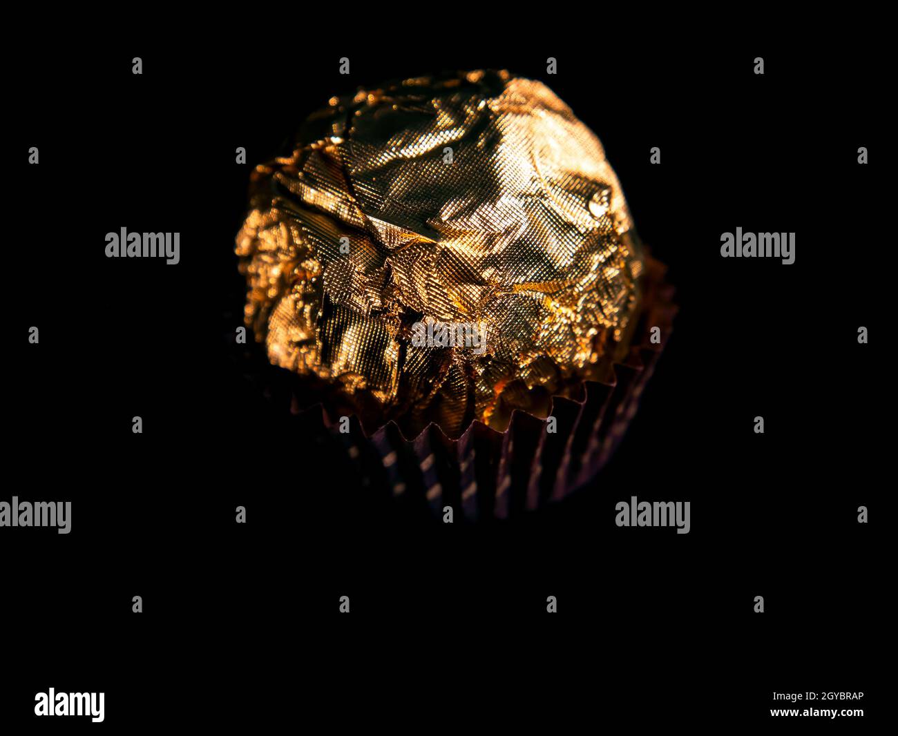 Round candies in golden foil on a black background. Wrapped chocolates ...