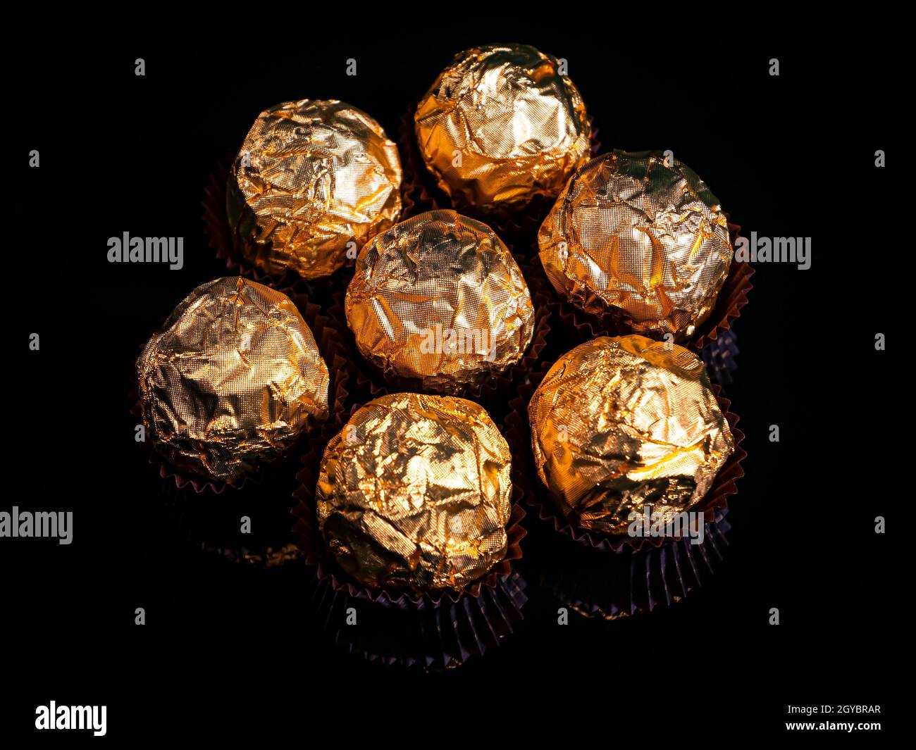 Round candies in golden foil on a black background. Wrapped chocolates ...