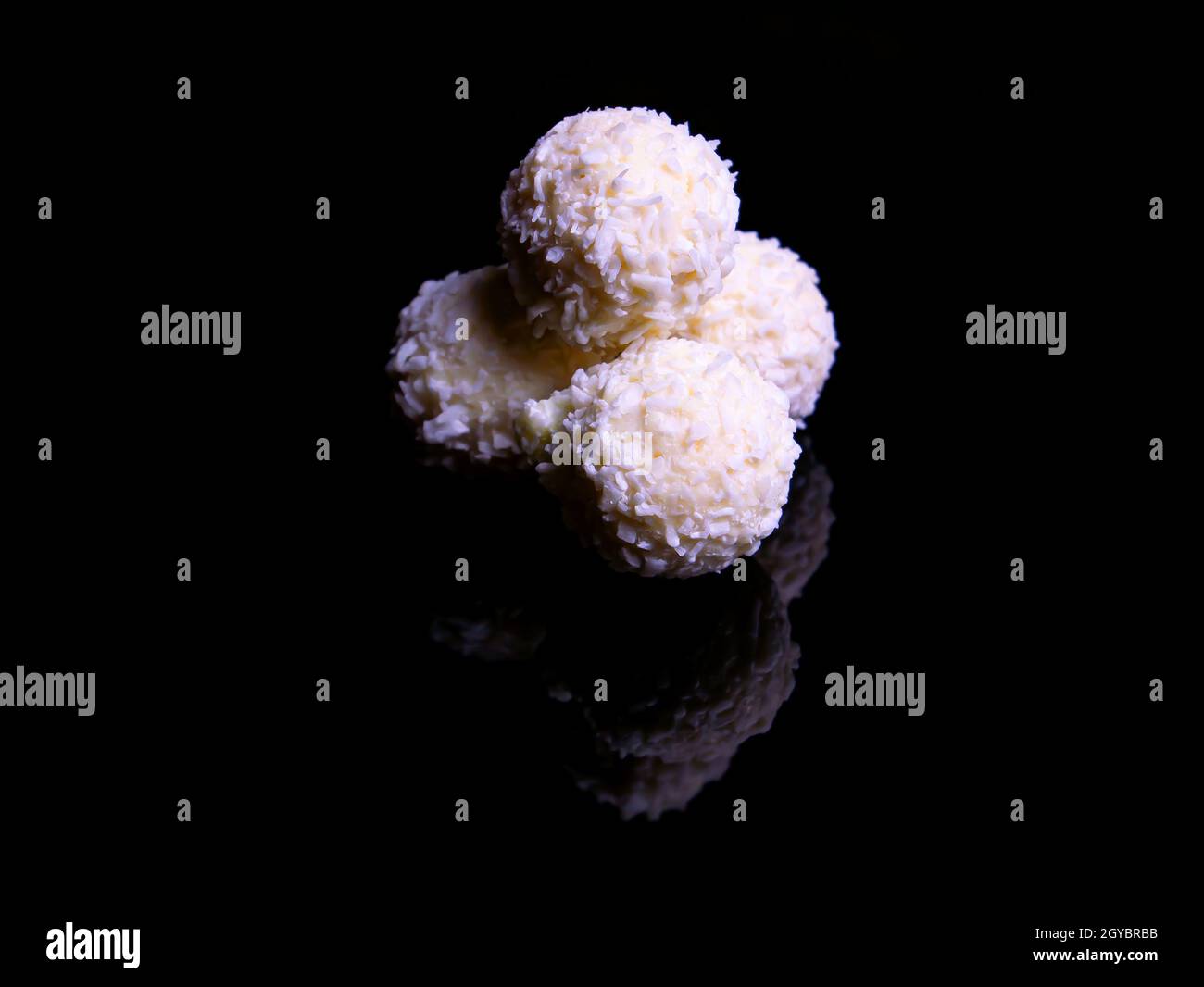 Round white candy with coconut flakes on a black background. Chocolate ...