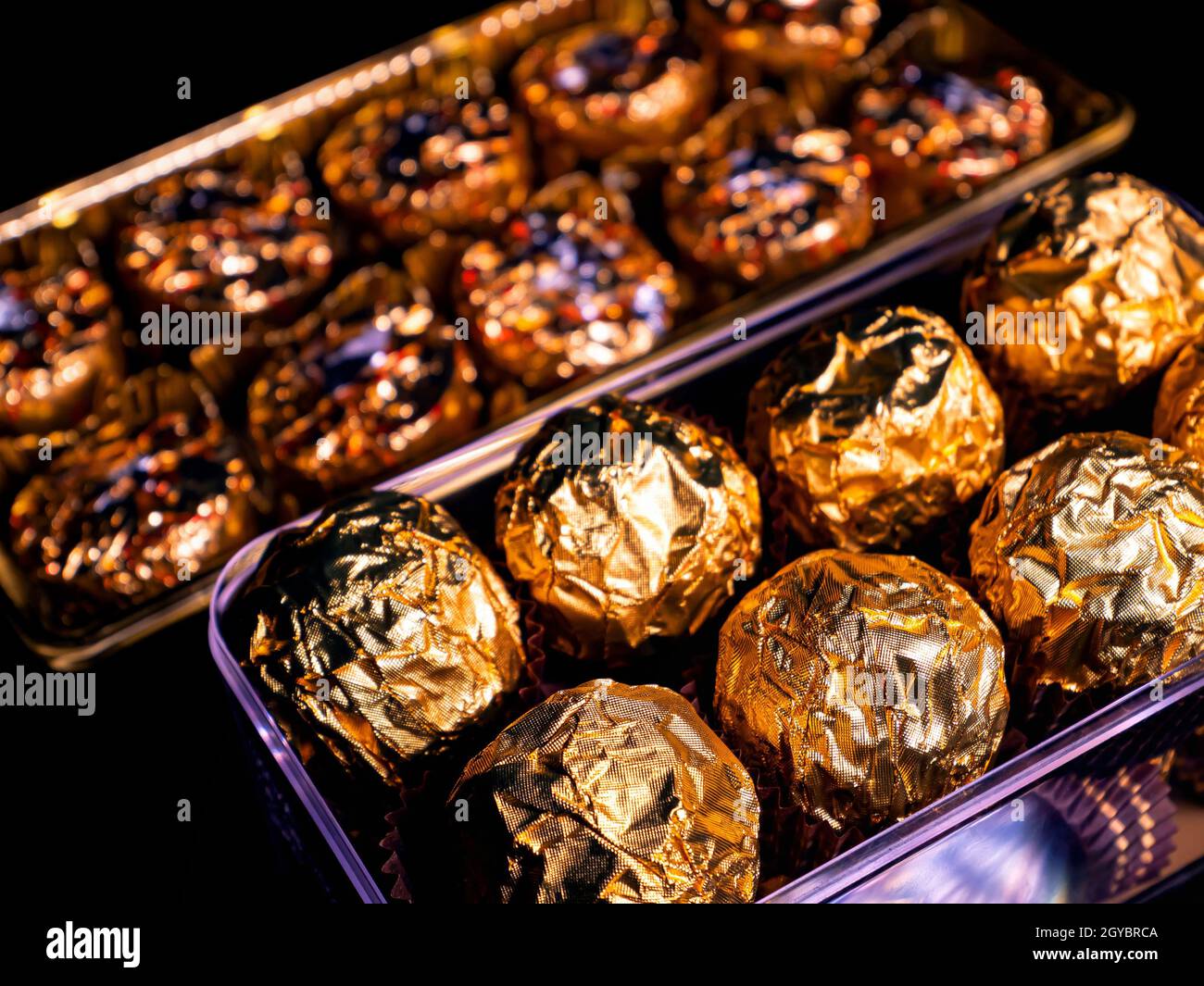 A box of round candies in golden foil on a black background. Wrapped ...