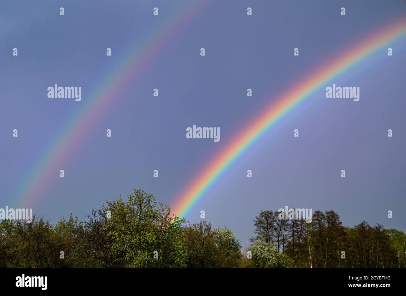 Two rainbows with rain clouds in the sky. Colored rainbow. Color spectrum. Rain clouds. Gloomy ...