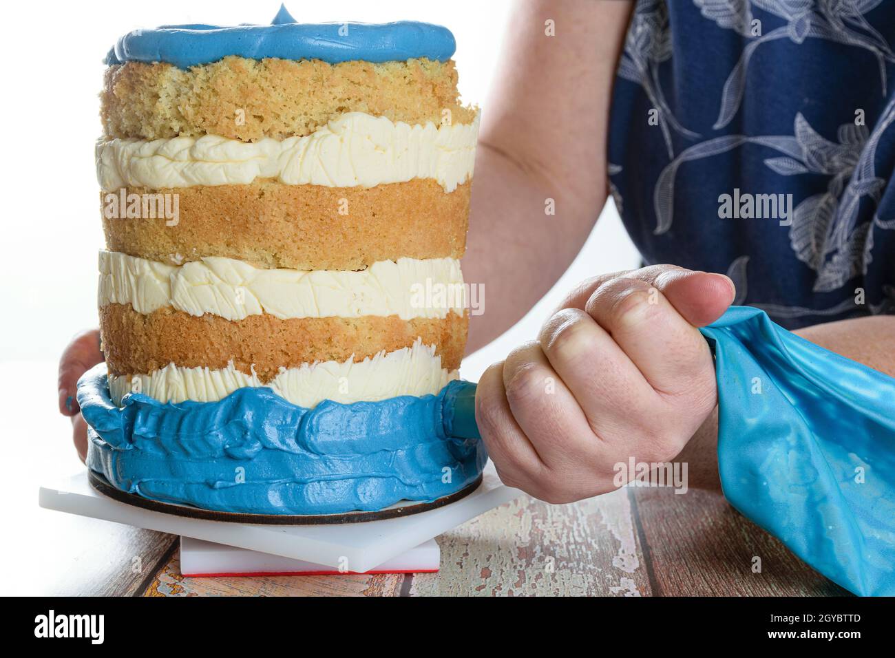 High key photo. Baker using a icing nozzle to put blue frosting on the ...
