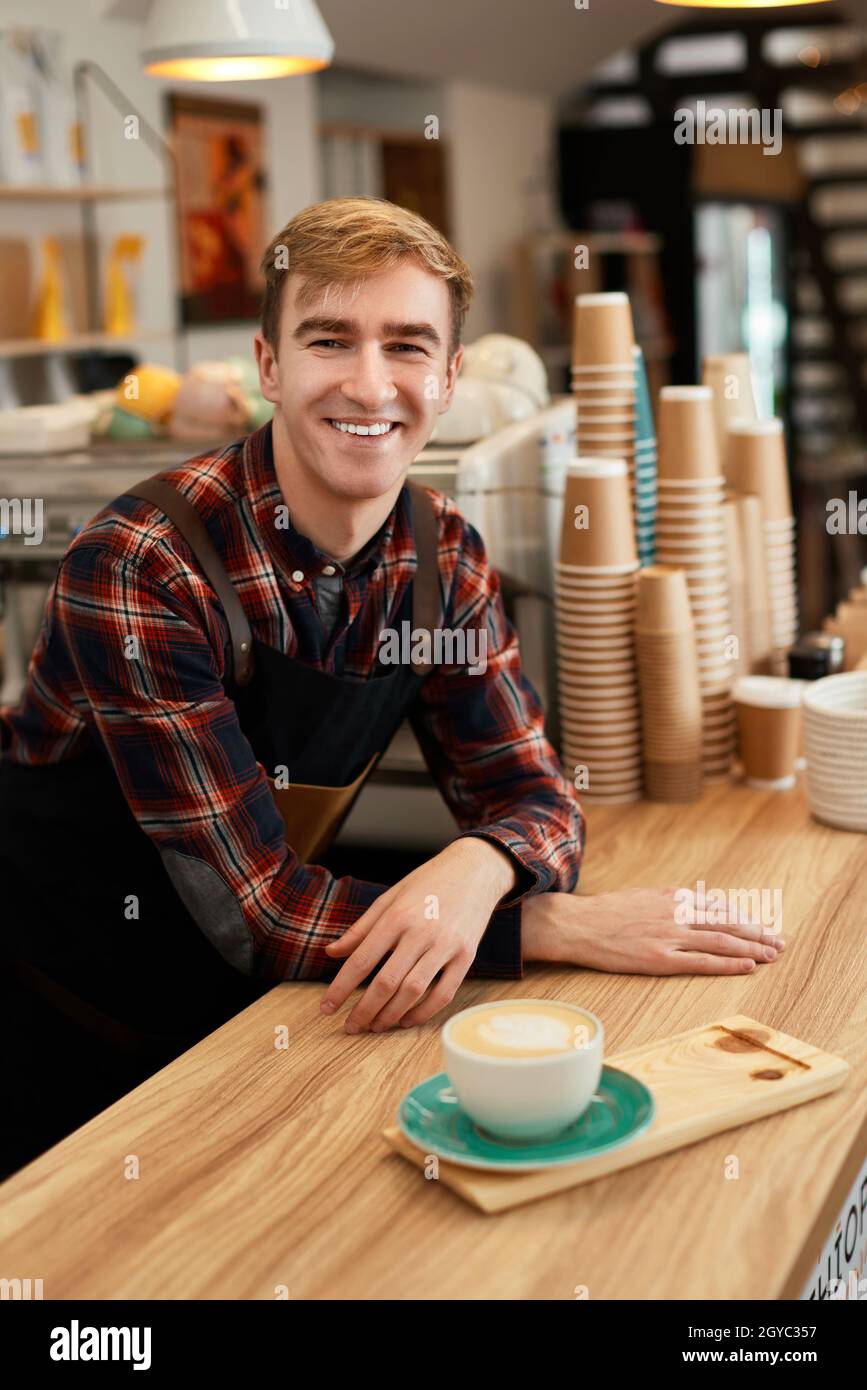 smiling male waiter in apron with cup of hot drink in coffee shop ...