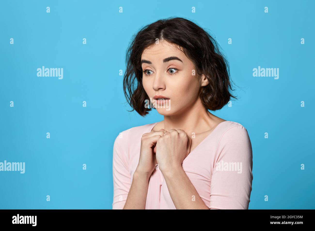 scared curly young brunette woman on blue background. Human emotions ...