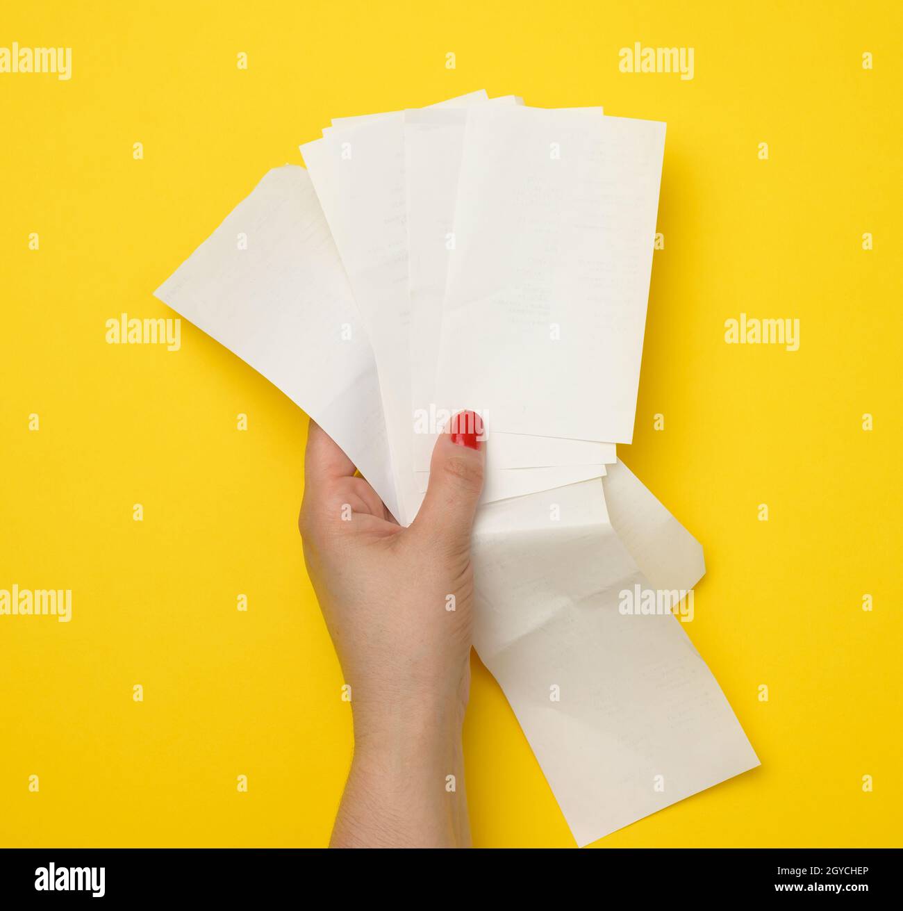female hand holds a stack of paper checks on a yellow background ...