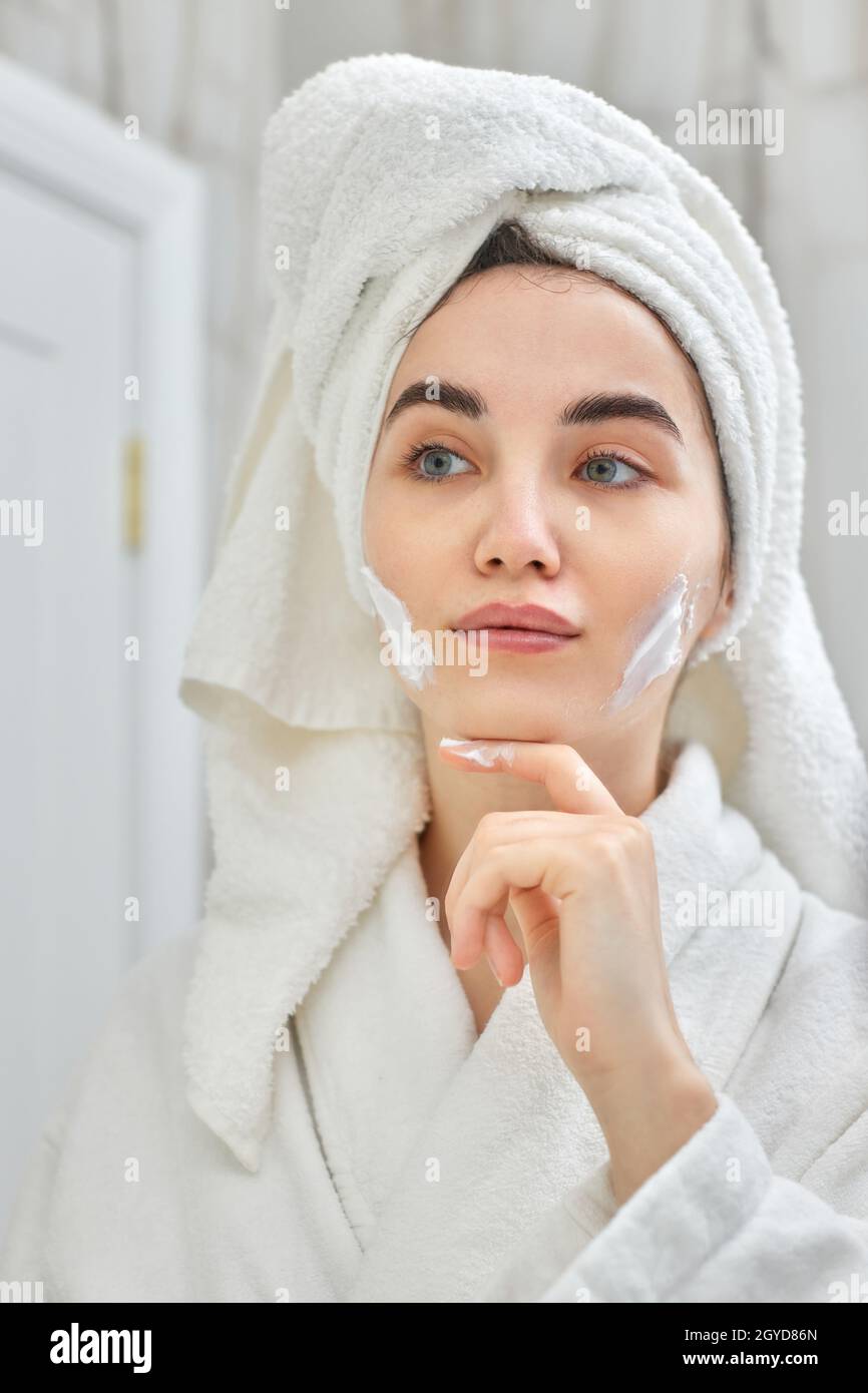 Beautiful Woman In White Bathrobes Applying Facial Cream In Front Of