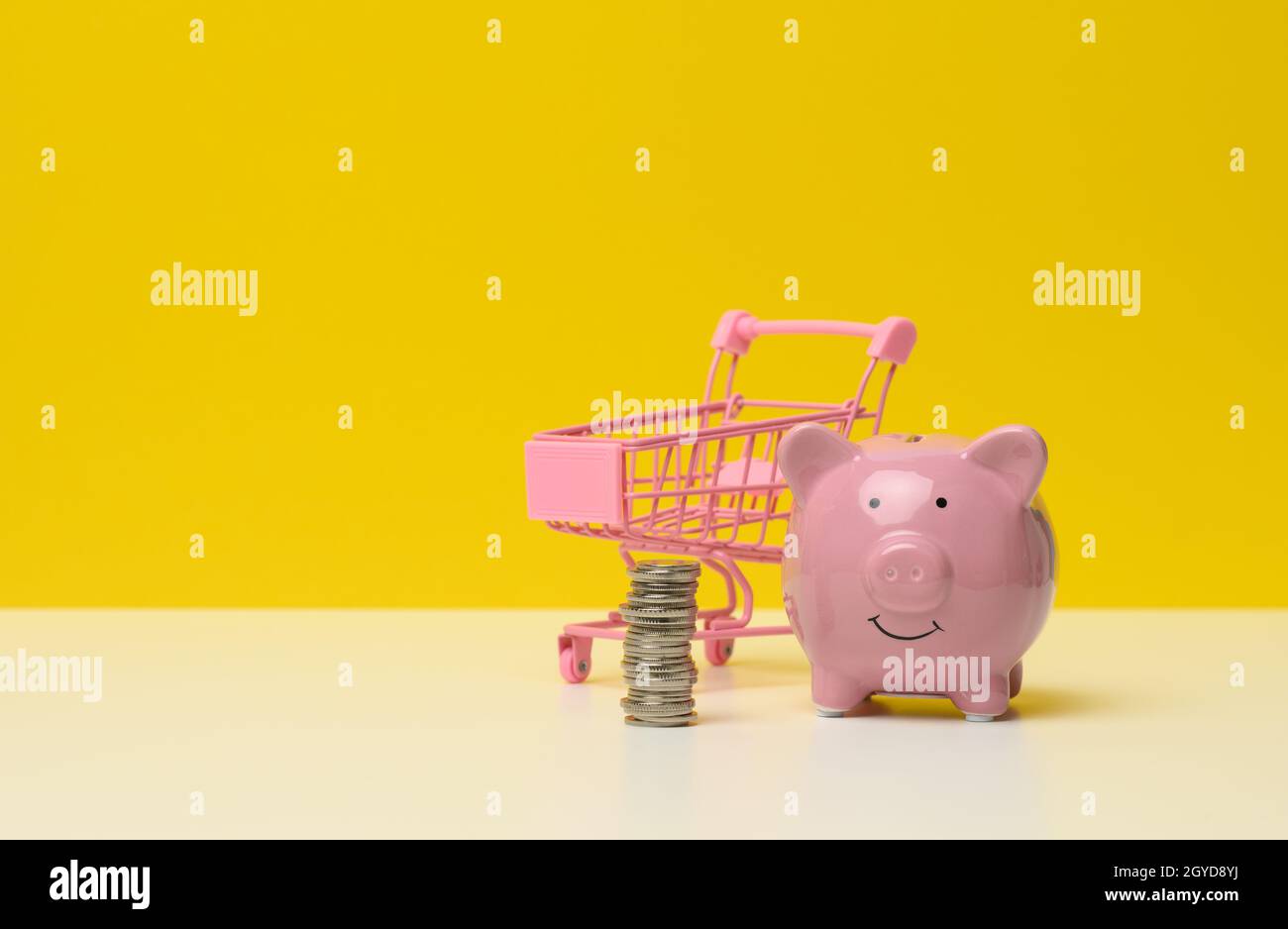 pink ceramic piggy bank and a stack of coins on a white table, yellow ...