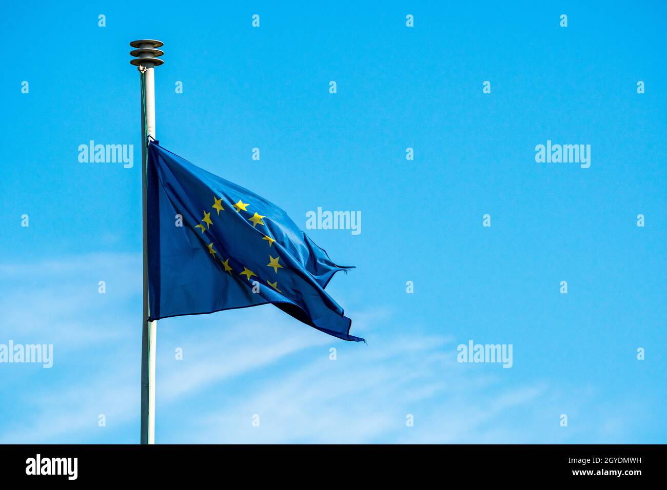 Looking up at the EU Flag on a flag pole waving in the wind, tattered ...