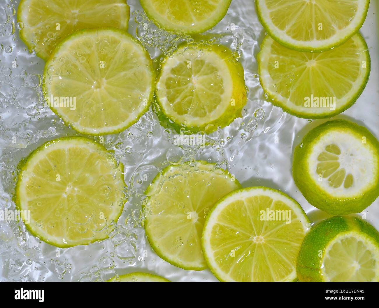Limes close-up in liquid with bubbles. Slices of green ripe limes in ...