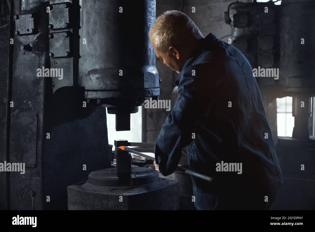 Qualified forge worker in overalls hitting molten metal. Mature man ...