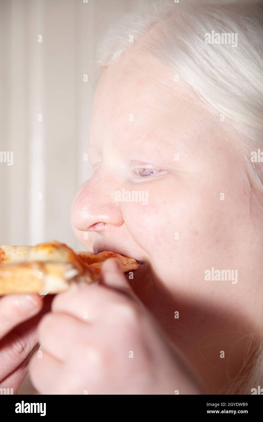 Albino woman eating a slice of pizza indoors Stock Photo - Alamy