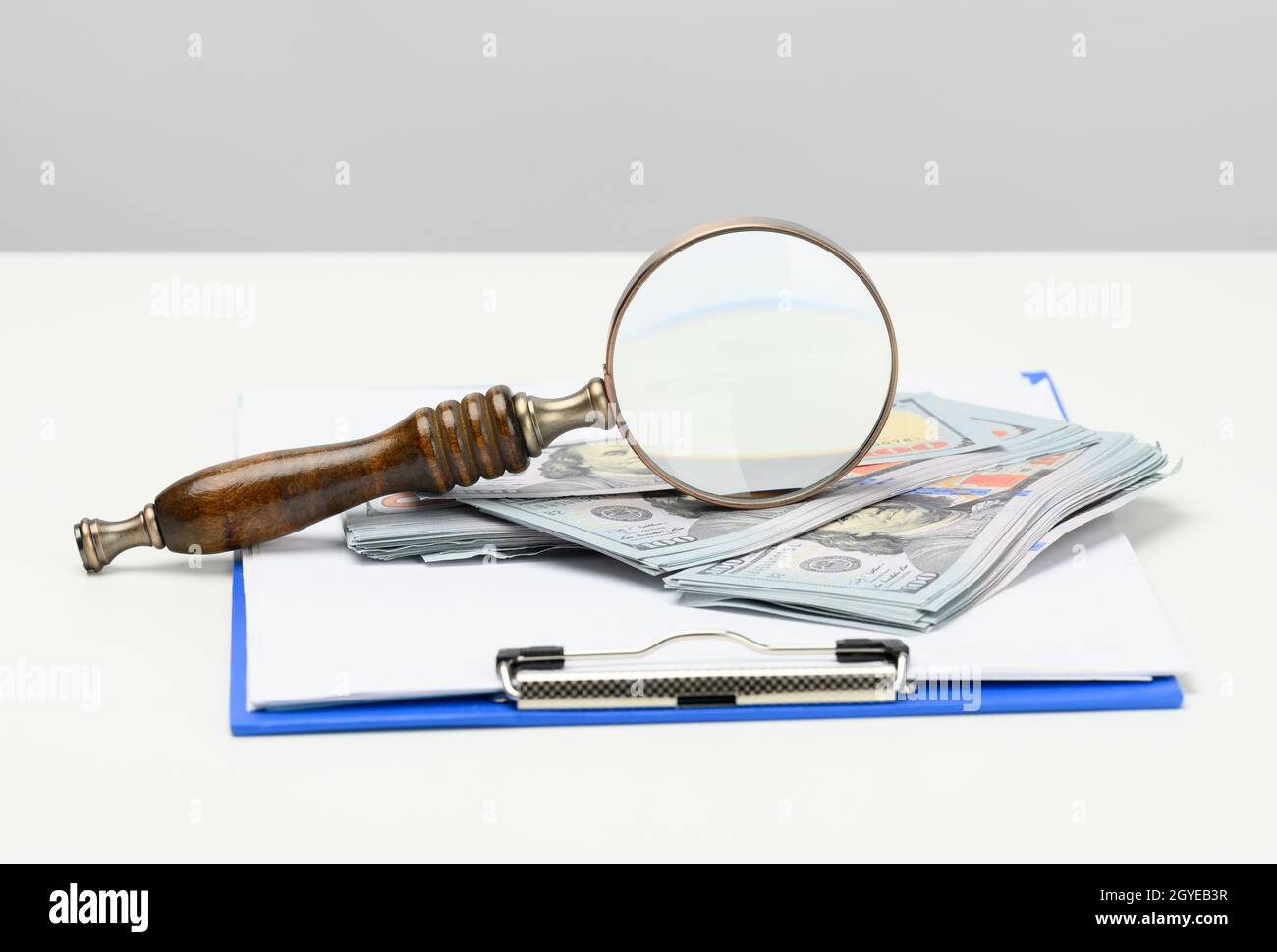 a stack of one hundred dollar bills and a wooden magnifier on a white ...