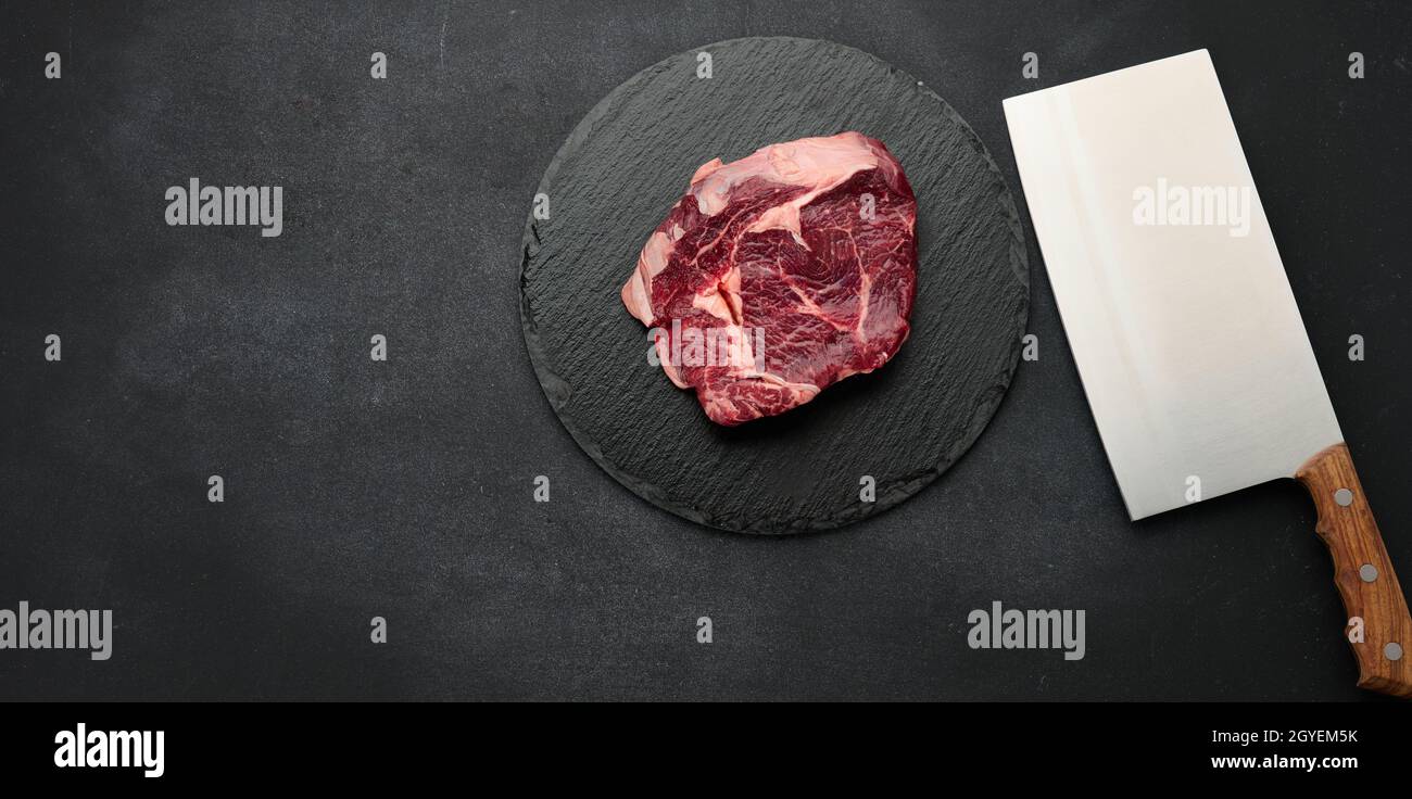 round raw piece of beef meat on a black board. Ribeye for barbecue, top ...