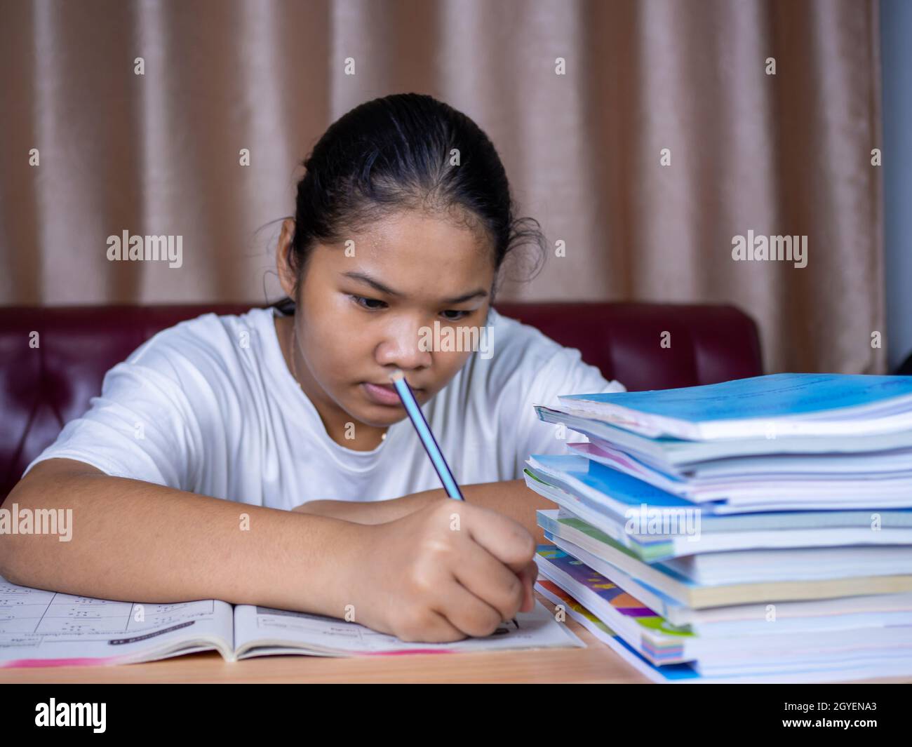 girl doing homework on a wooden table and there was a pile of books ...