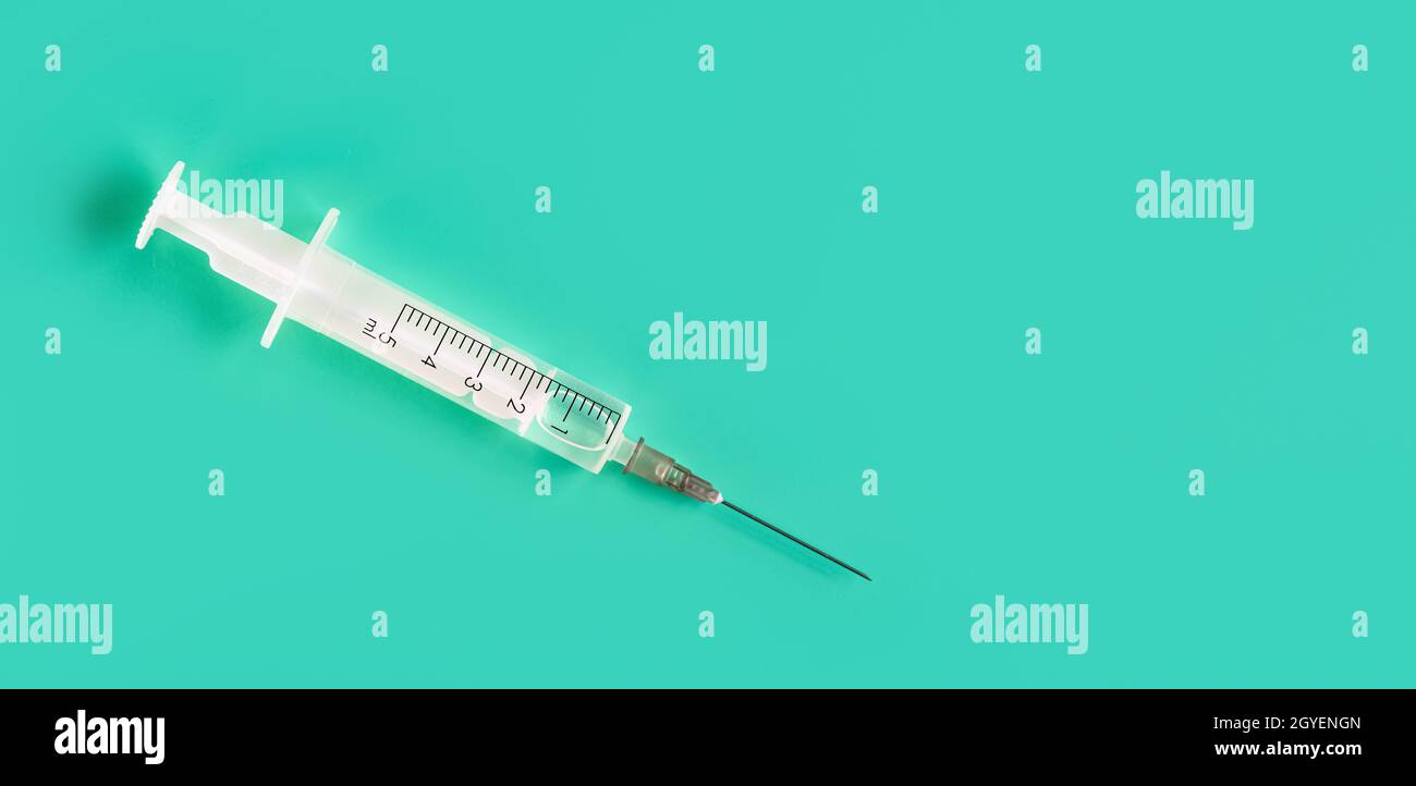 White injection syringe and needle with clear liquid on a green blue ...