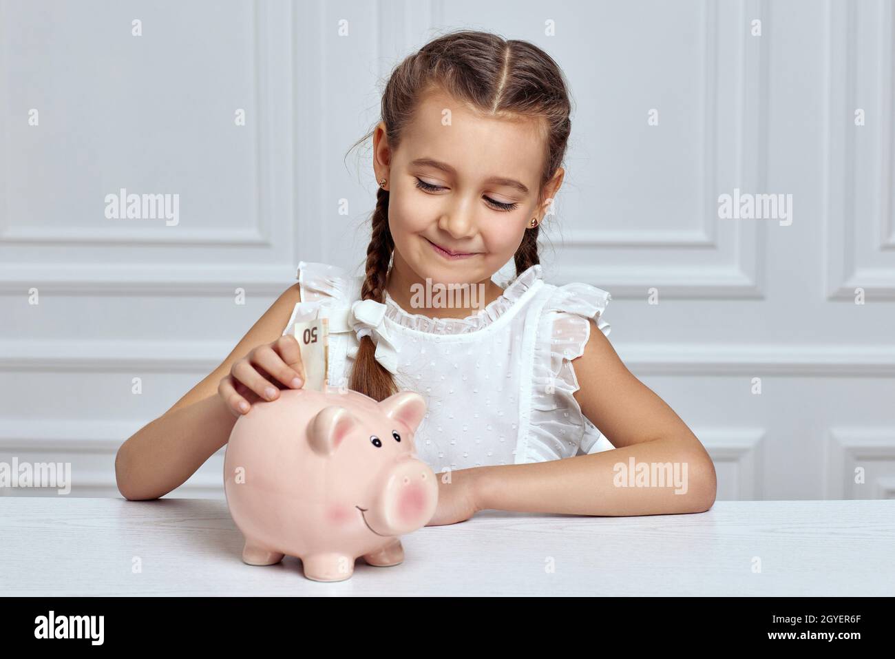 cute little girl putting banknotes into pink piggy bank. child saving ...