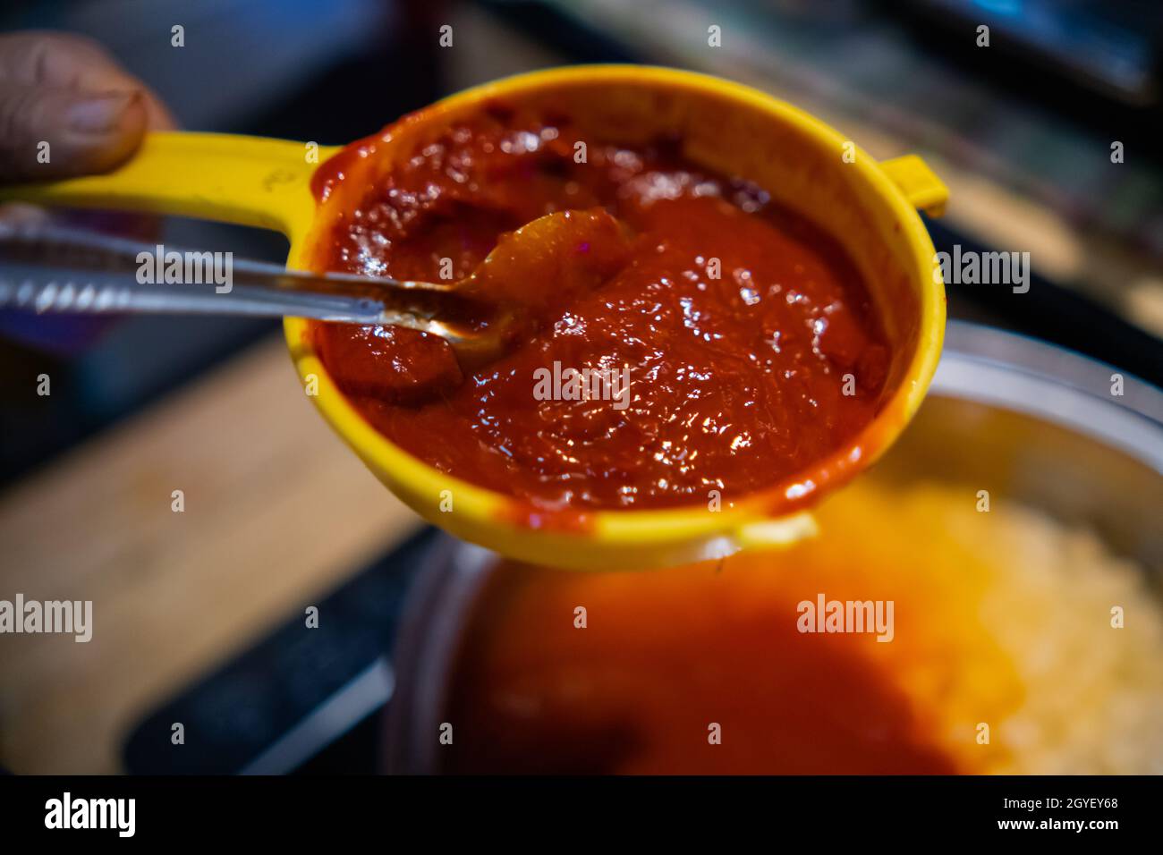 Red chili pepper paste in plastic strainer above cooking pot Stock ...