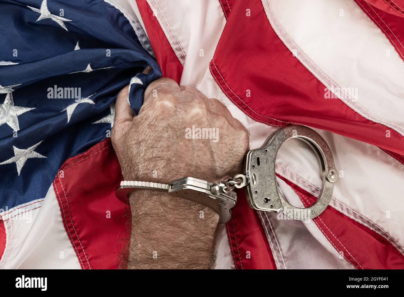 A man in handcuffs grasps the American flag in frustration and anger as ...