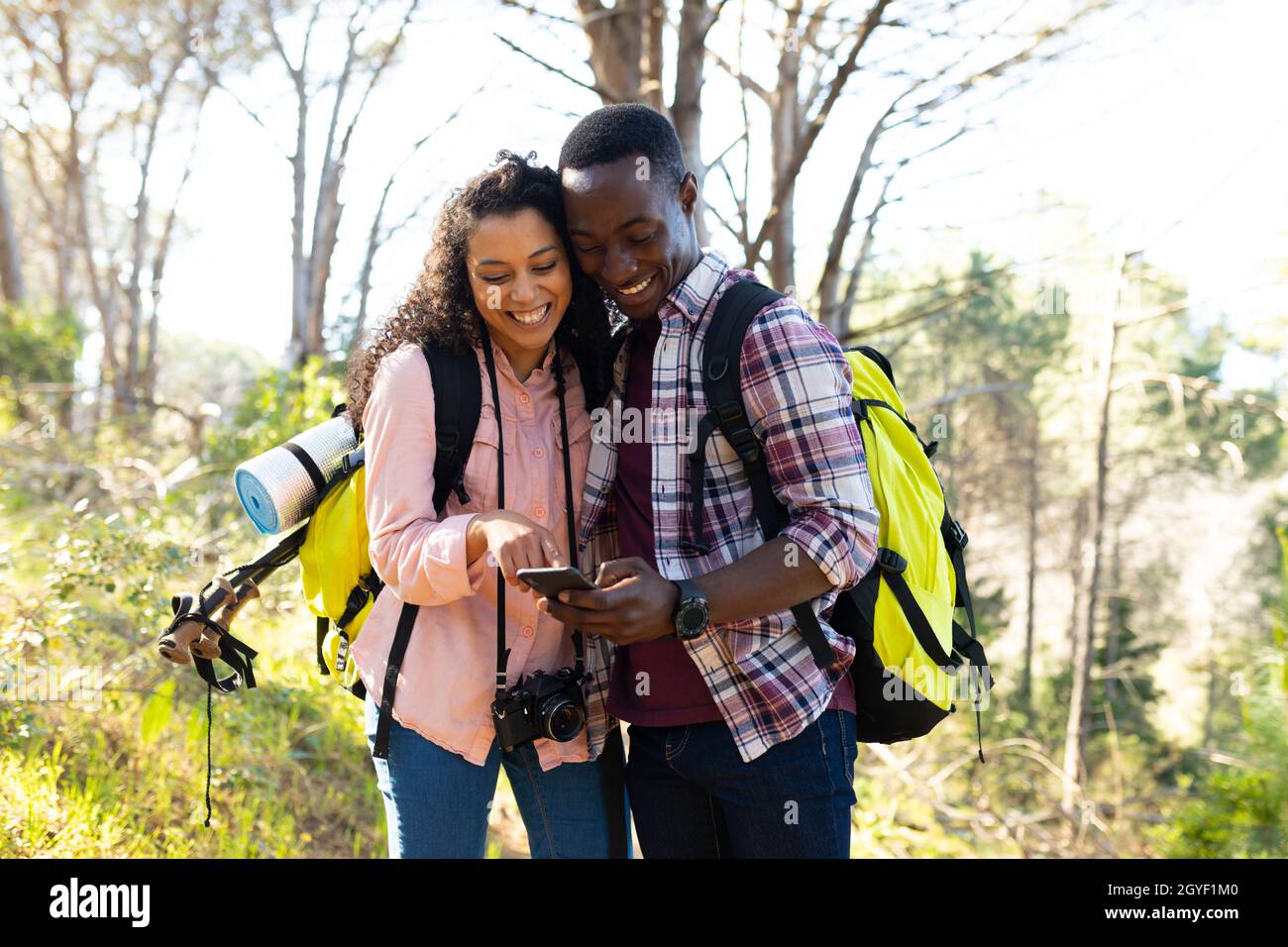 Happy diverse couple with backpacks using smartphone hiking in ...