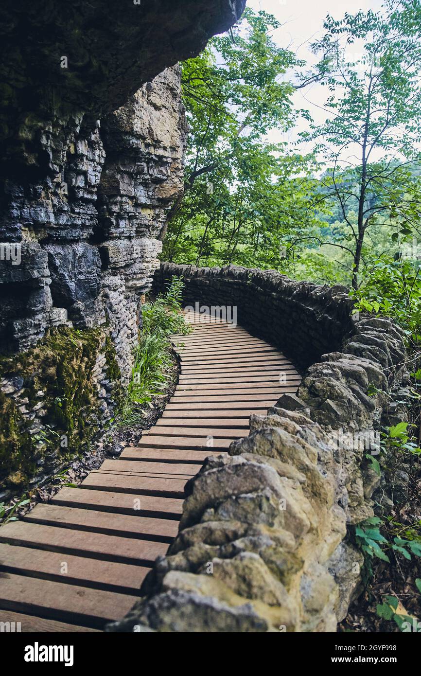 Beautiful wood boardwalk with stone wall against rock cliffs covered in ...