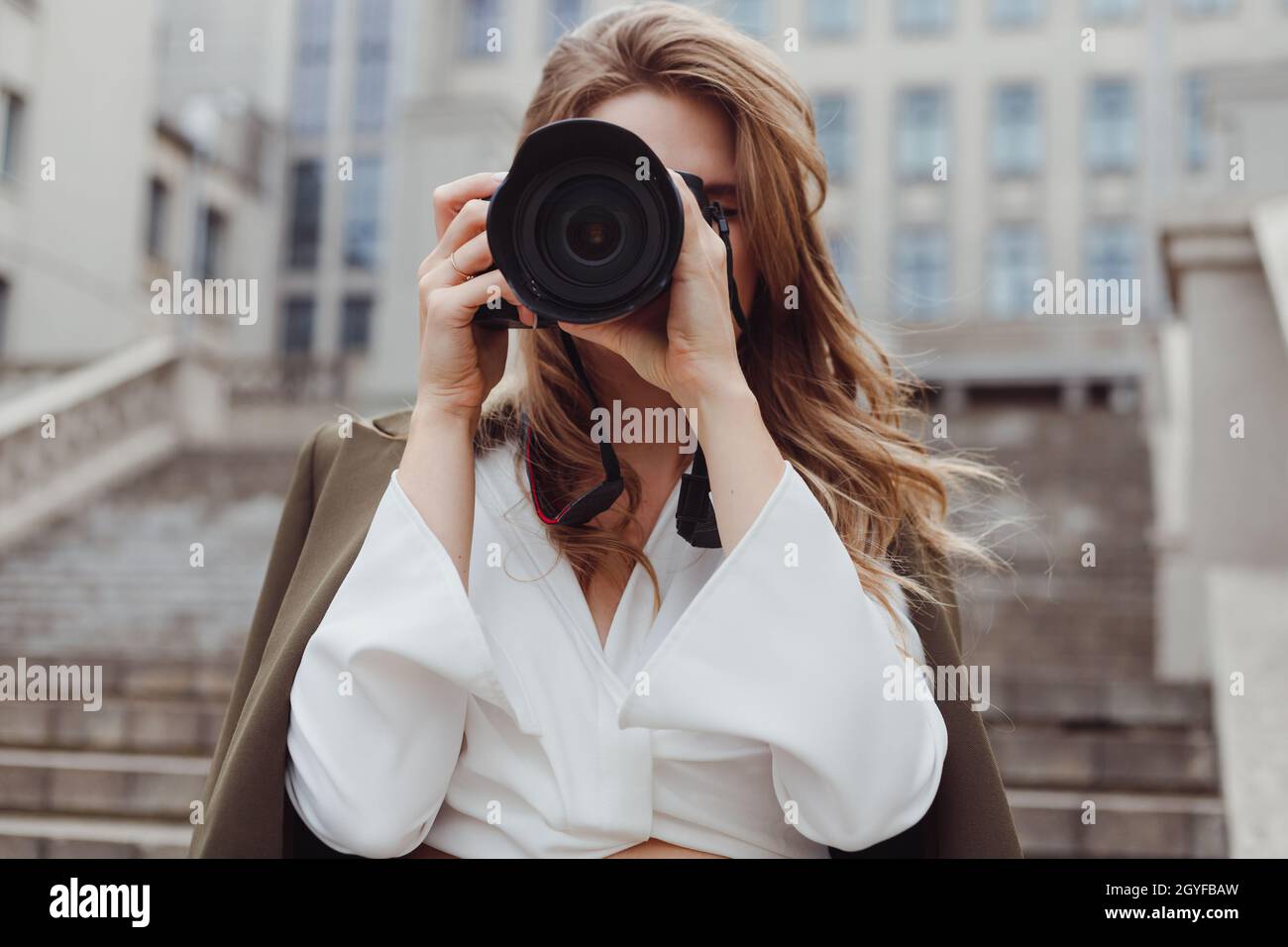 Portrait of woman photographer covering her face with camera outdoors ...