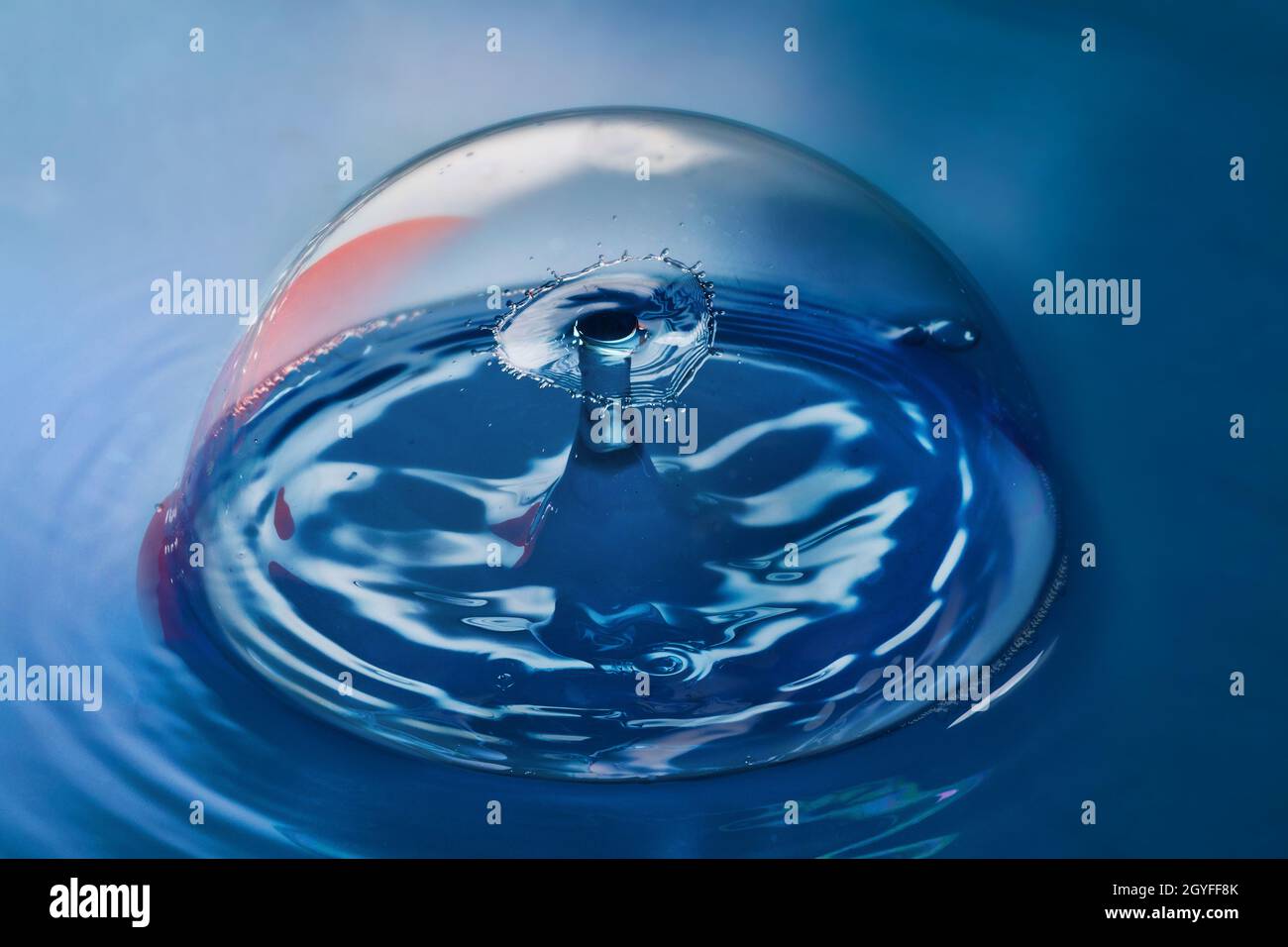 Bubble on blue surface with ripples of water drops crashing together ...