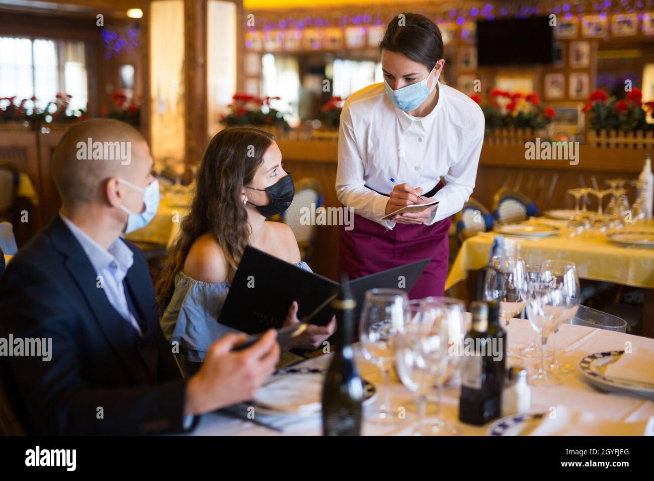 Woman waiter in protective mask is taking order from clients in ...