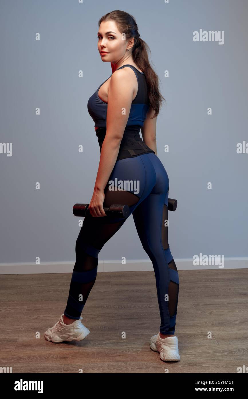 Portrait of a fitness model working out with dumbbells on grey ...