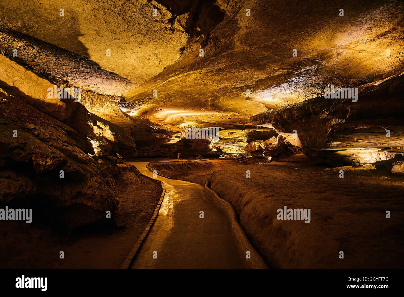 Walking path through large tourist cave with orange lights Stock Photo ...