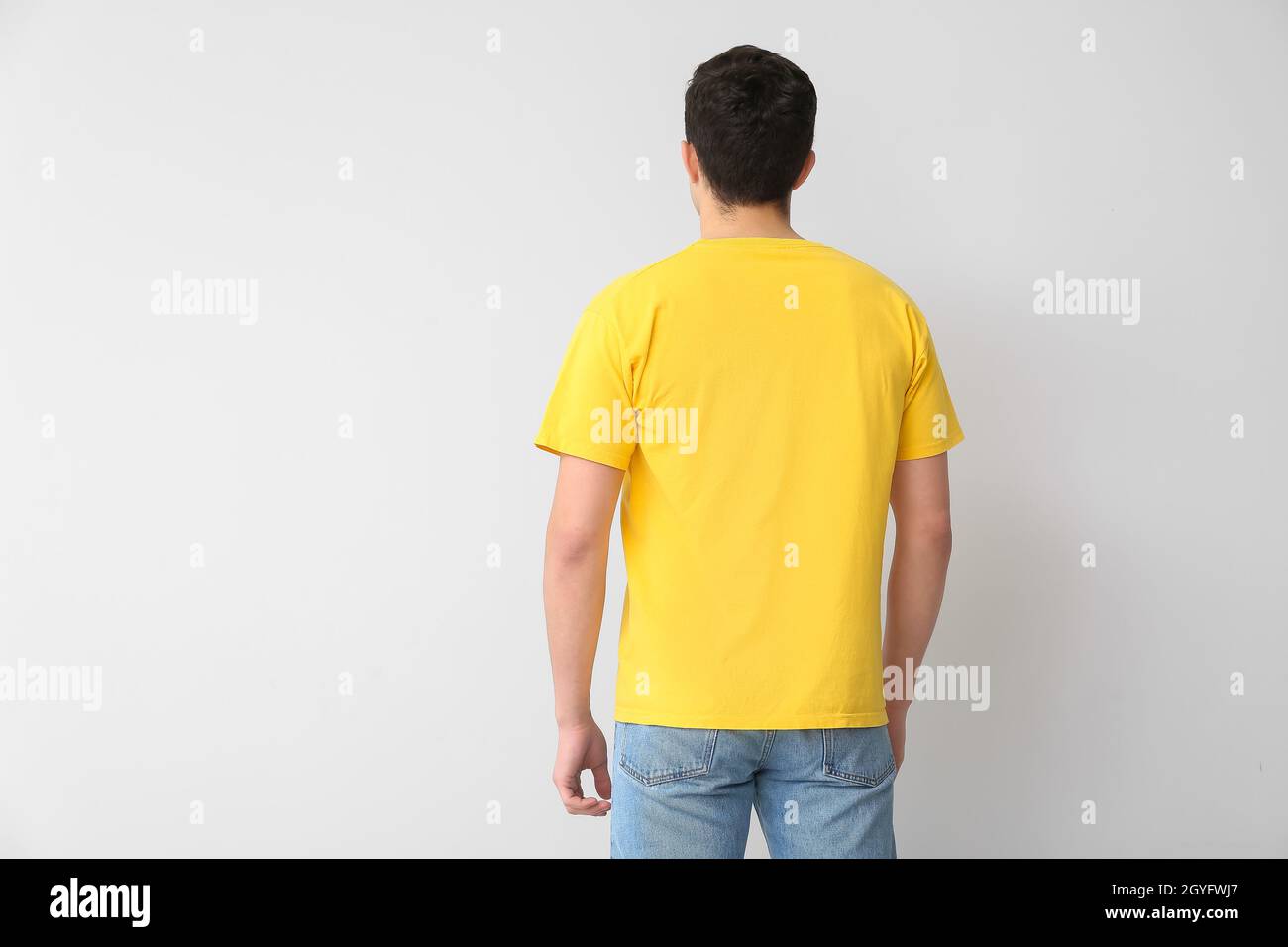 Handsome young man in stylish t-shirt on light background, back view ...