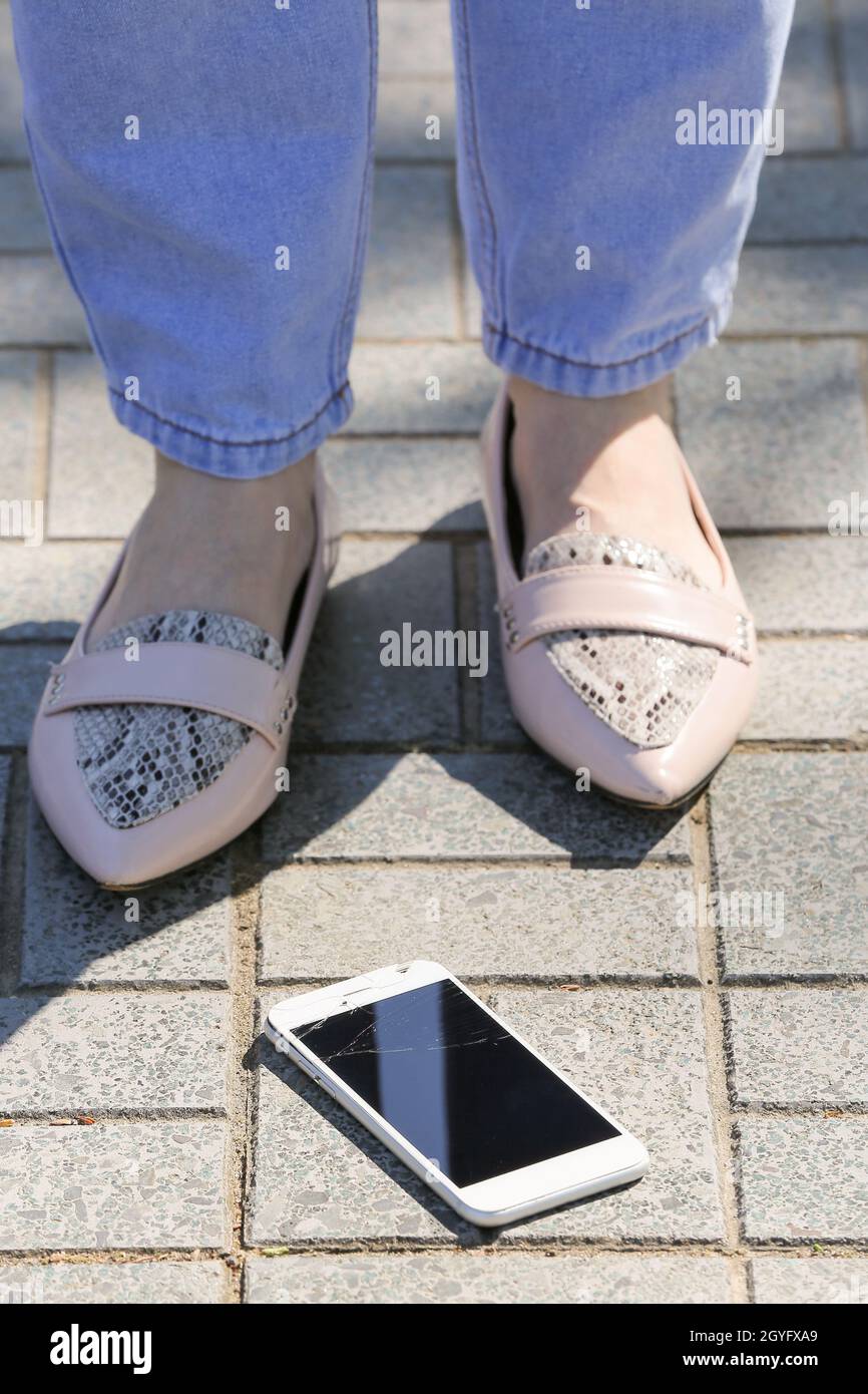 Legs of woman and damaged mobile phone on pavement outdoors, closeup ...