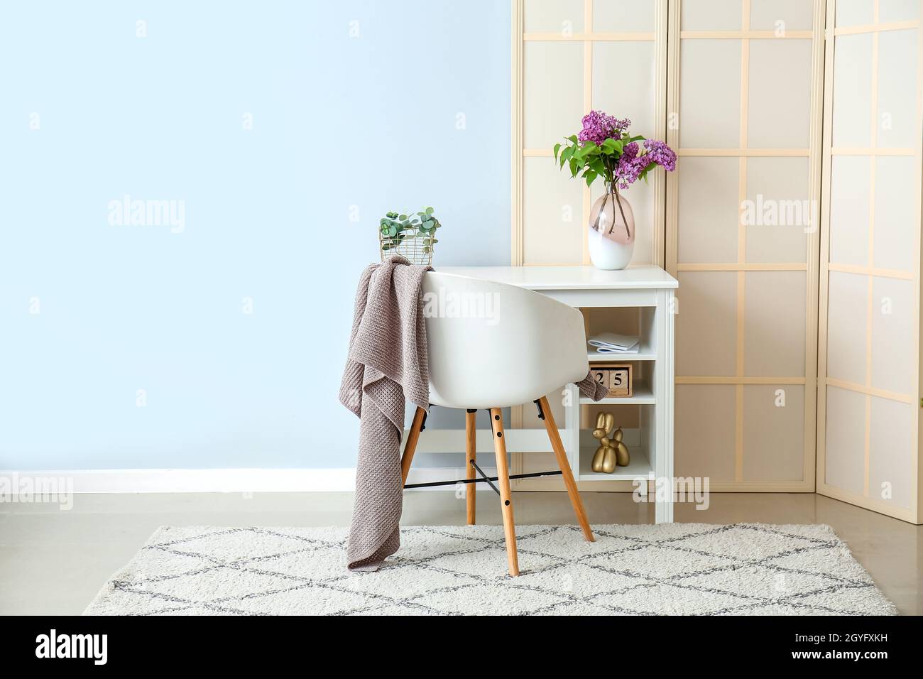 Desk with lilac flowers in vase and folding screen near blue wall Stock ...