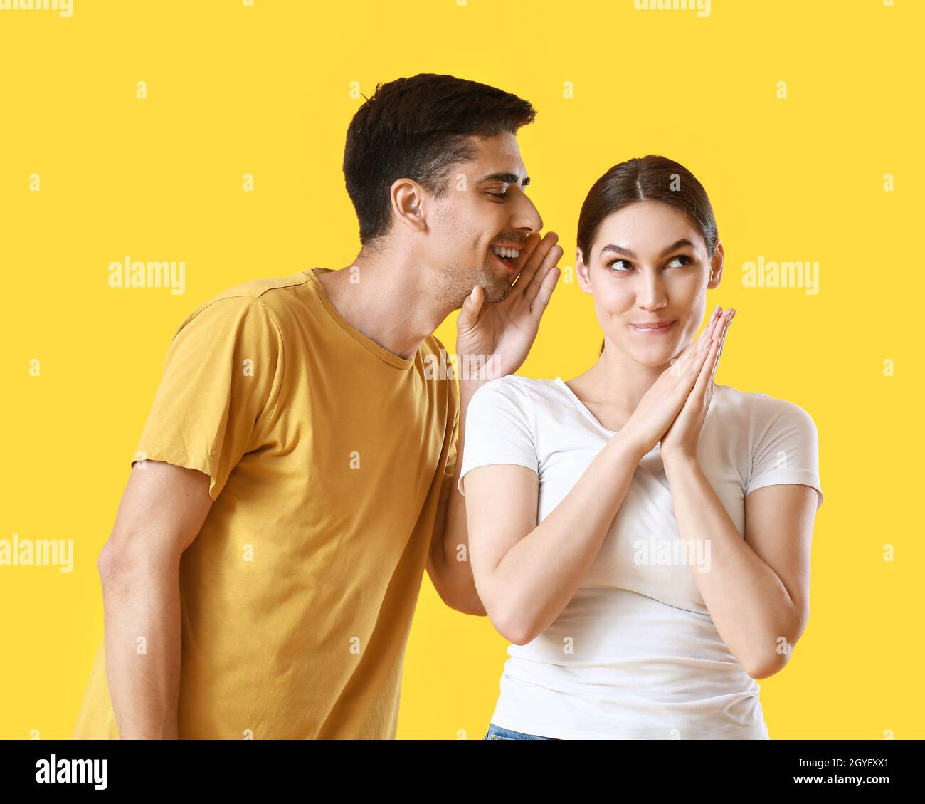 Young man sharing gossip with his wife on yellow background Stock Photo ...