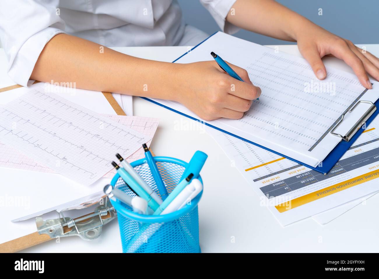 Woman doctor taking notes on clipboard while sitting at her table in ...