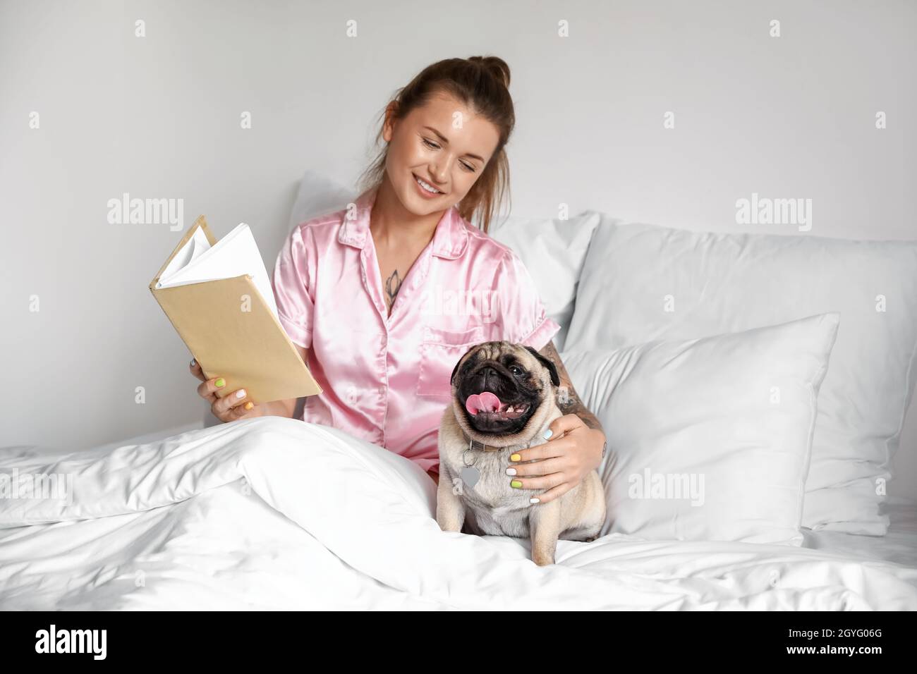 Young woman with cute pug dog reading book in bedroom Stock Photo - Alamy