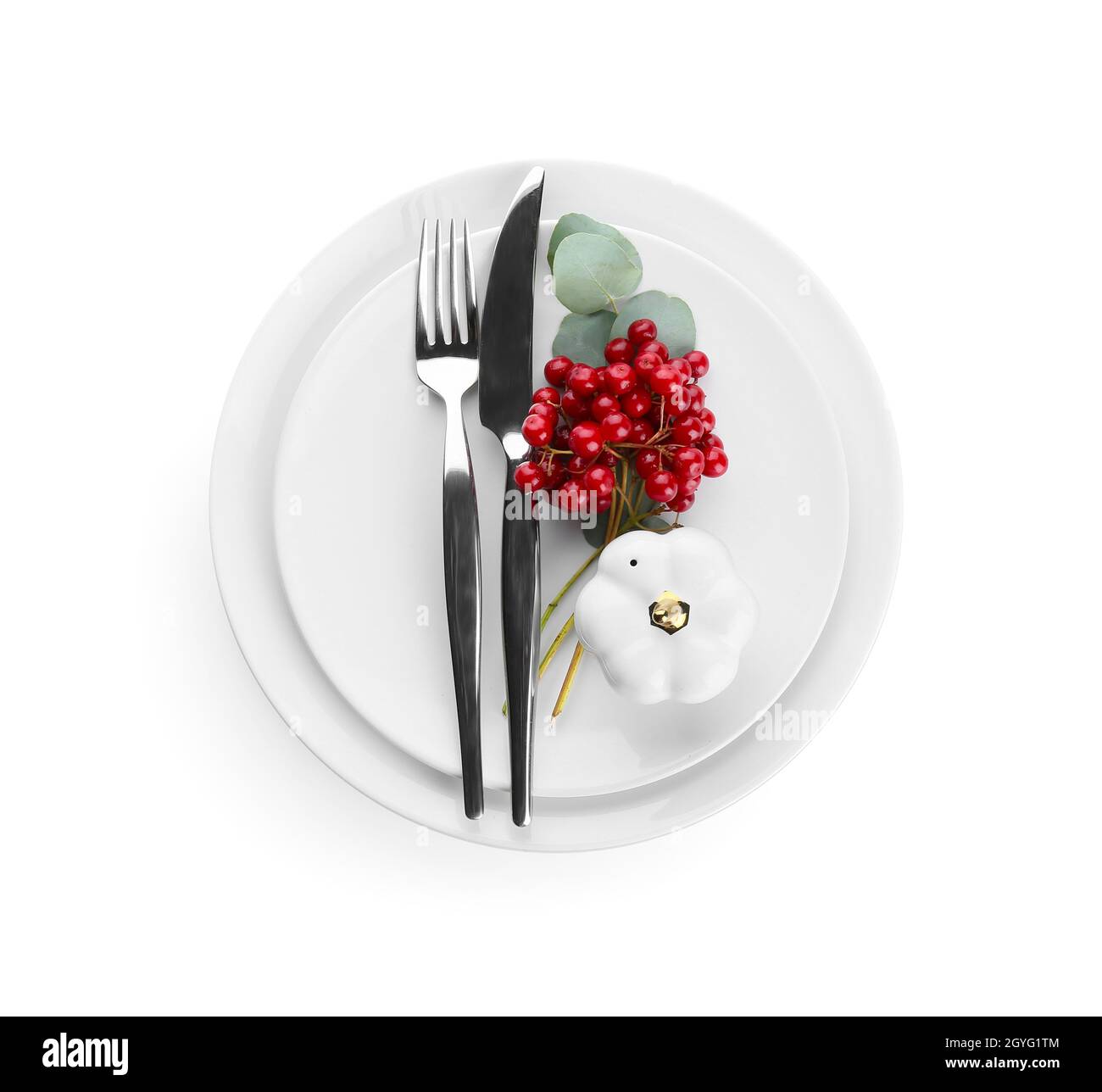 Thanksgiving table setting with pumpkin pepper shakers, cutlery, rowan and eucalyptus branch on ...