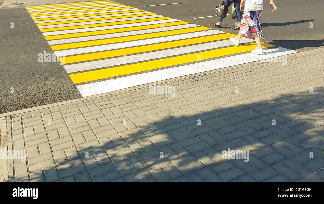 two pedestrians crossing the road on a new yellow-white marking of a ...