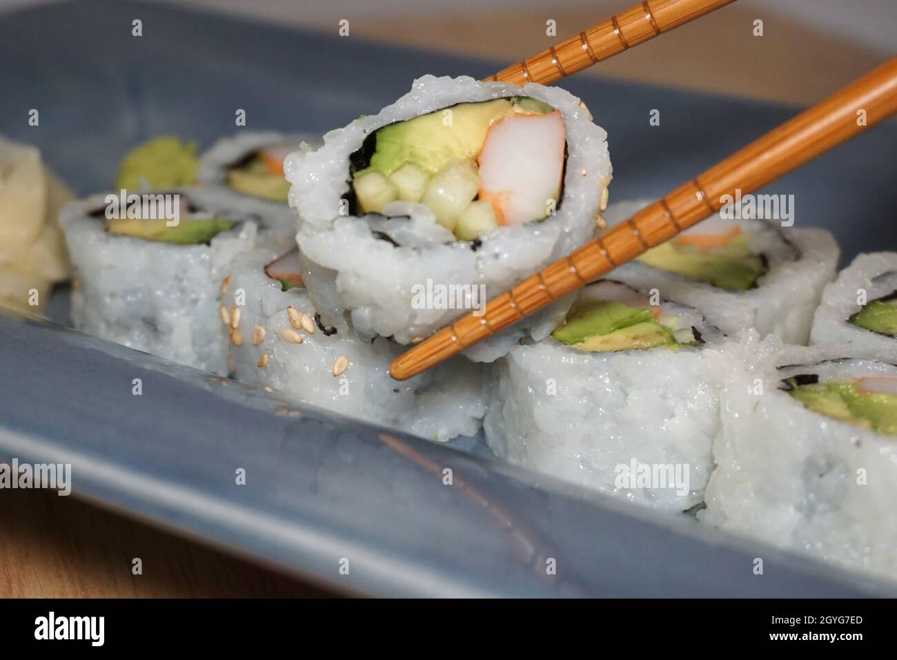 Picking up a piece of California maki sushi roll with chopsticks Stock Photo - Alamy