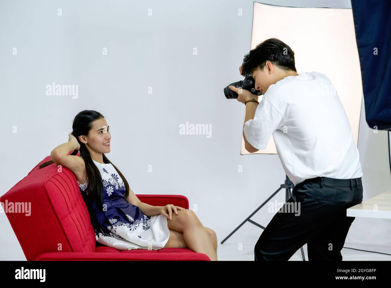 Young asian photographer is photographing a model posing on a red sofa ...