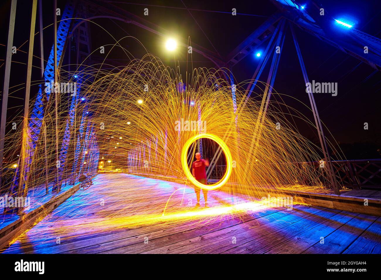 Ghostly man in middle of a ring of yellow sparks at night on a bridge ...