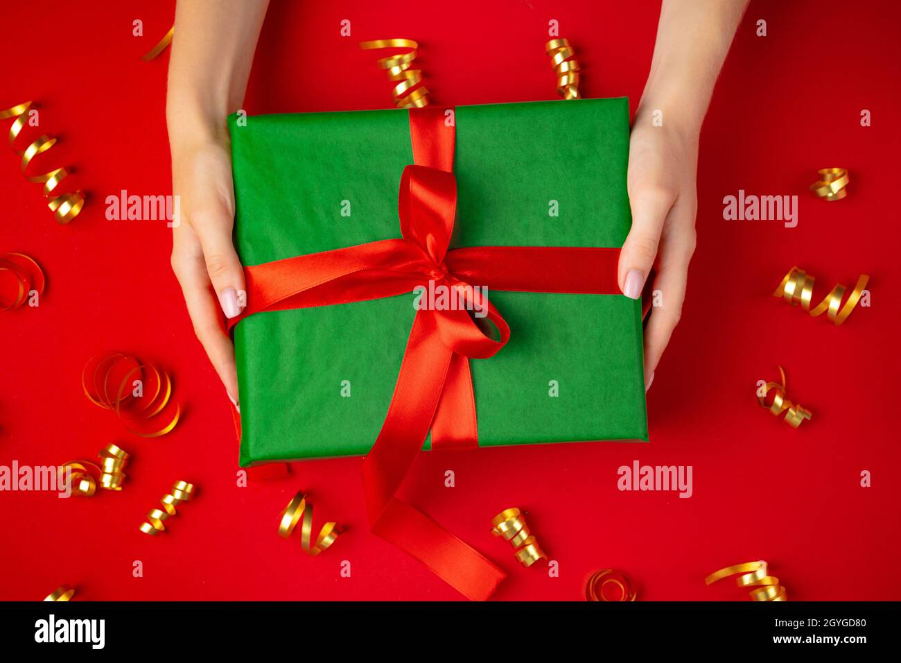 Female hands holding present on a red background Stock Photo - Alamy