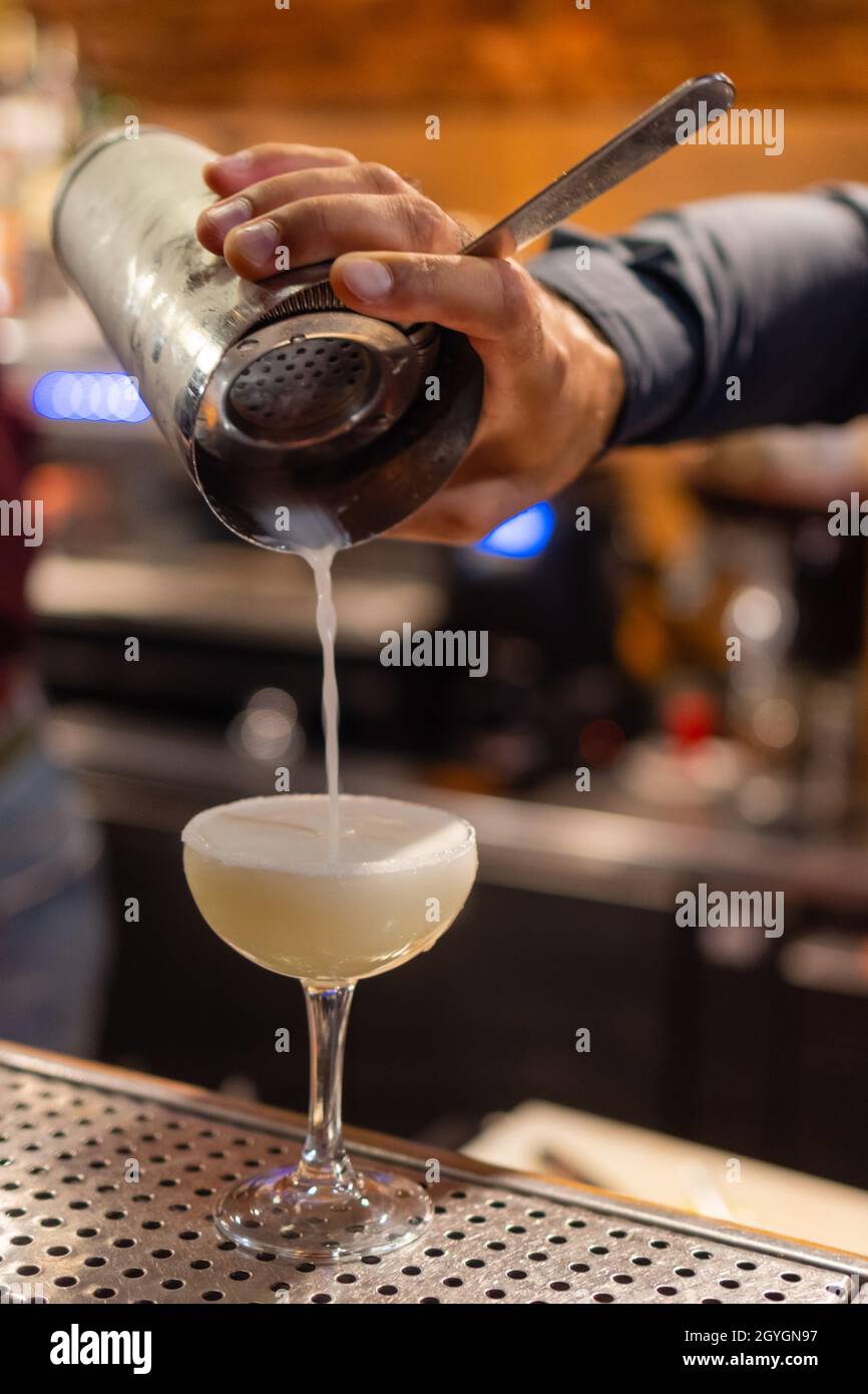 The bartender makes a cocktail at the bar, pours a glass of the shaker ...