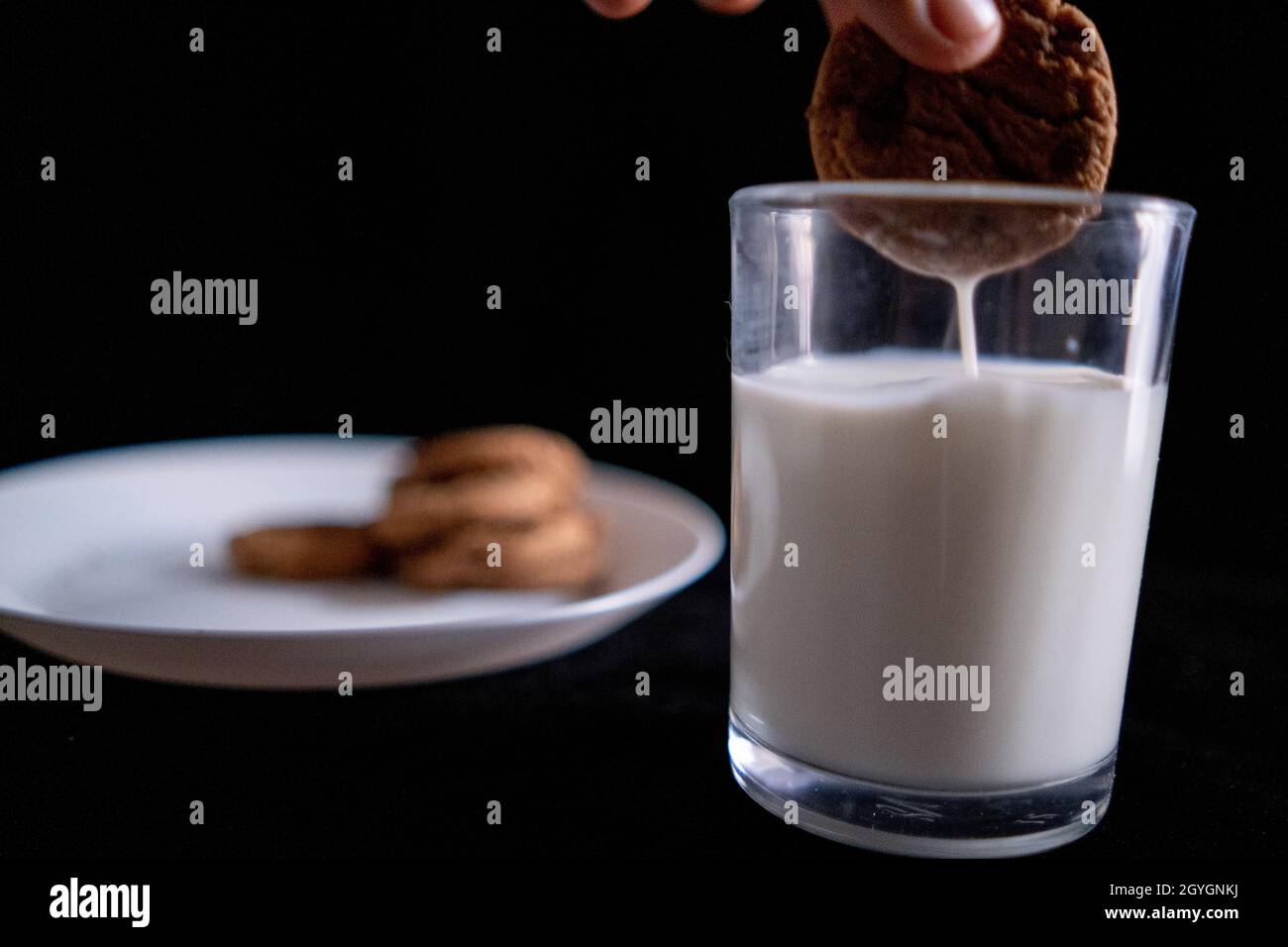 Hand dunking a cookie in glass of milk with black background Stock ...