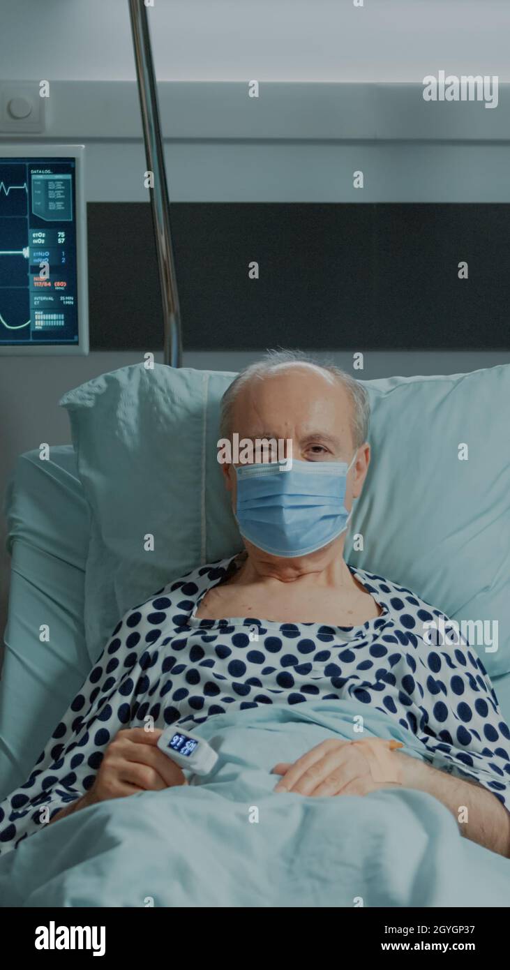 Portrait of old patient with face mask sitting in hospital ward ...