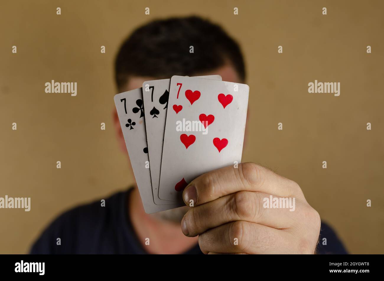 An adult male holds playing cards in front of his face. Hand with three ...