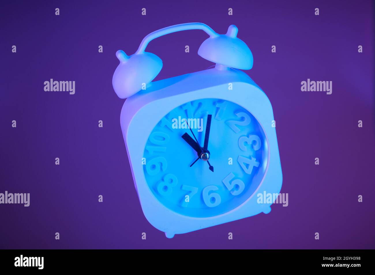 Light blue alarm clock suspended in air on a bright purple background ...