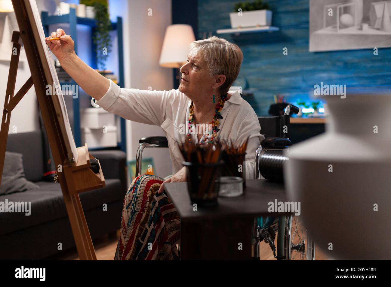 Old woman drawing on canvas using pencil while sitting in wheelchair at ...